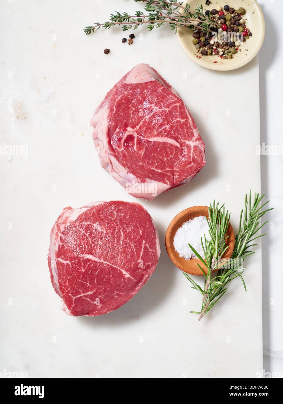 Raw chuck tender steak sits on a marble cutting board. Salt, pepper ...