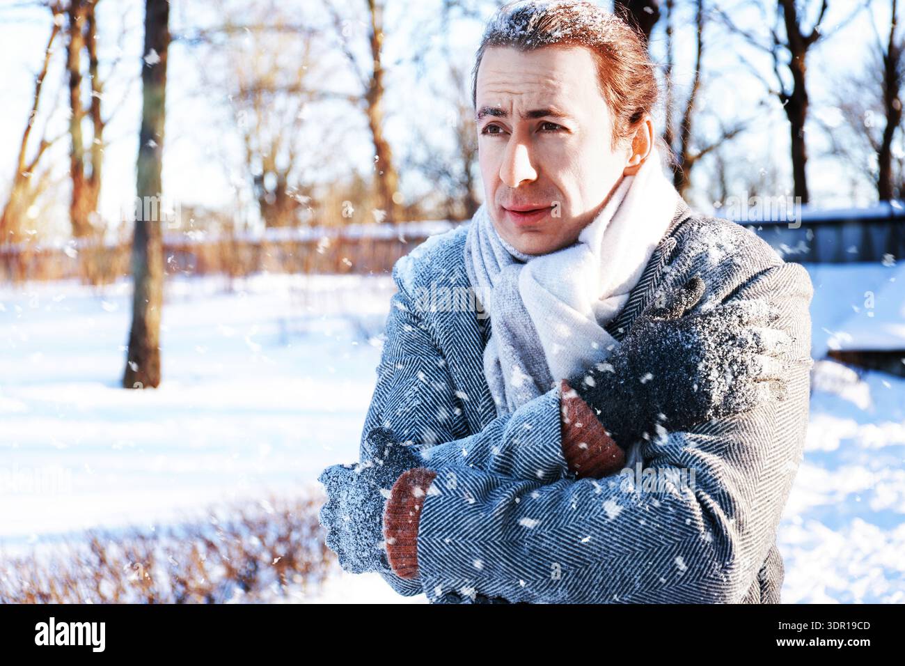 Frozen man shivering in a winter park, hugging himself to warm up ...