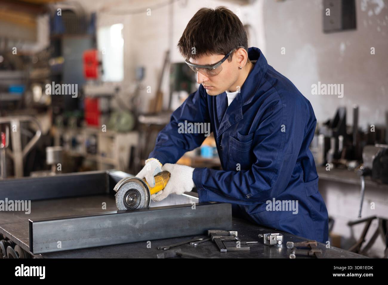 Young guy polishing metal part in workshop Stock Photo - Alamy