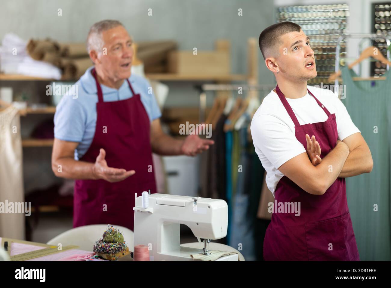Elderly man scolding young man in sewing workshop Stock Photo - Alamy