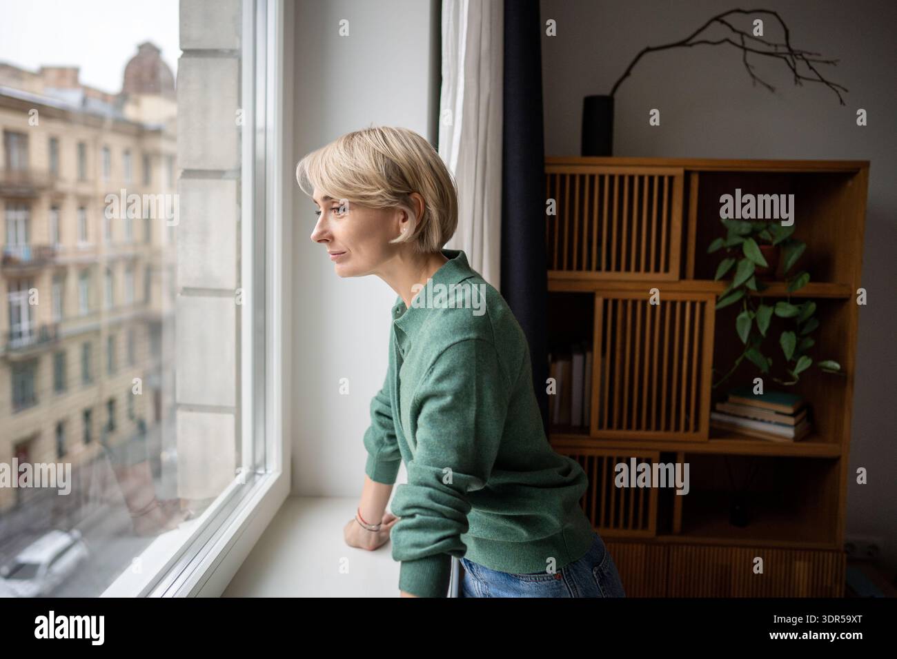 Smiling cheerful woman looking outside window enjoying morning city ...