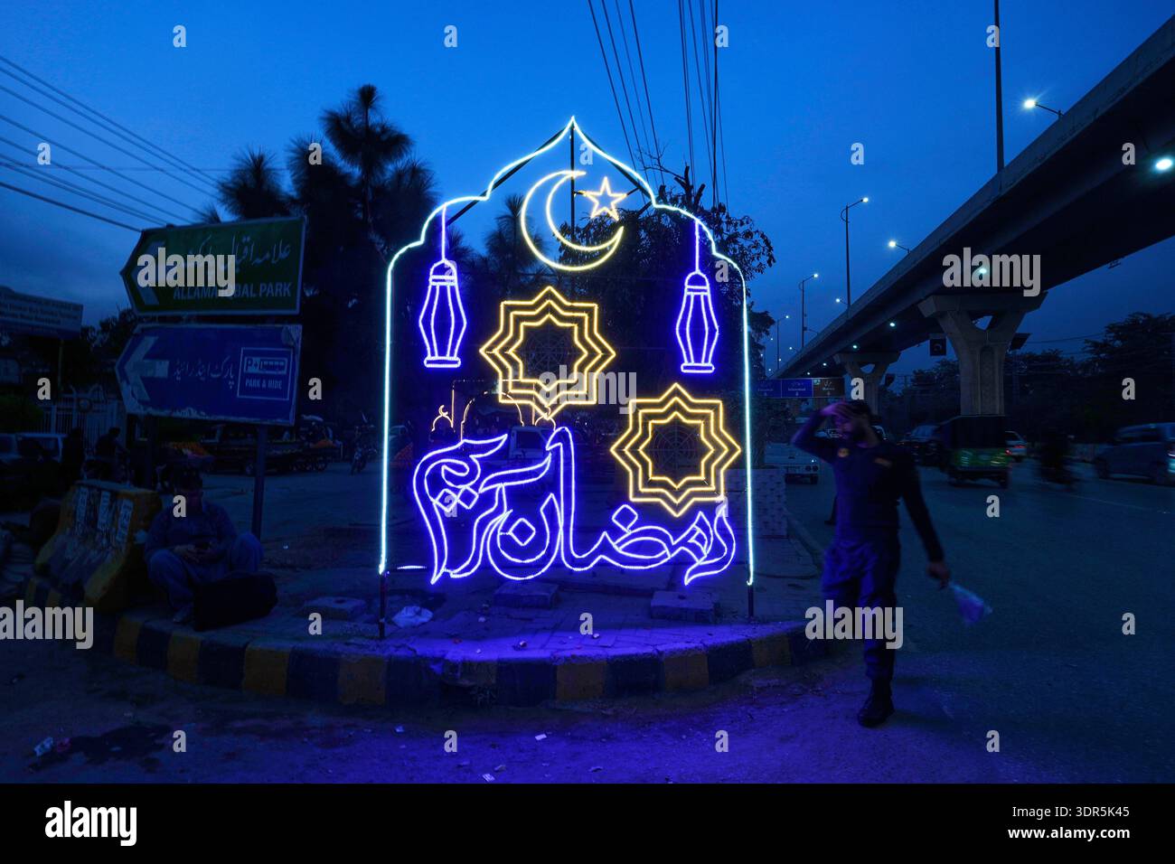 A man walks past a neon light decoration with wording 'Ramadan Kareem ...