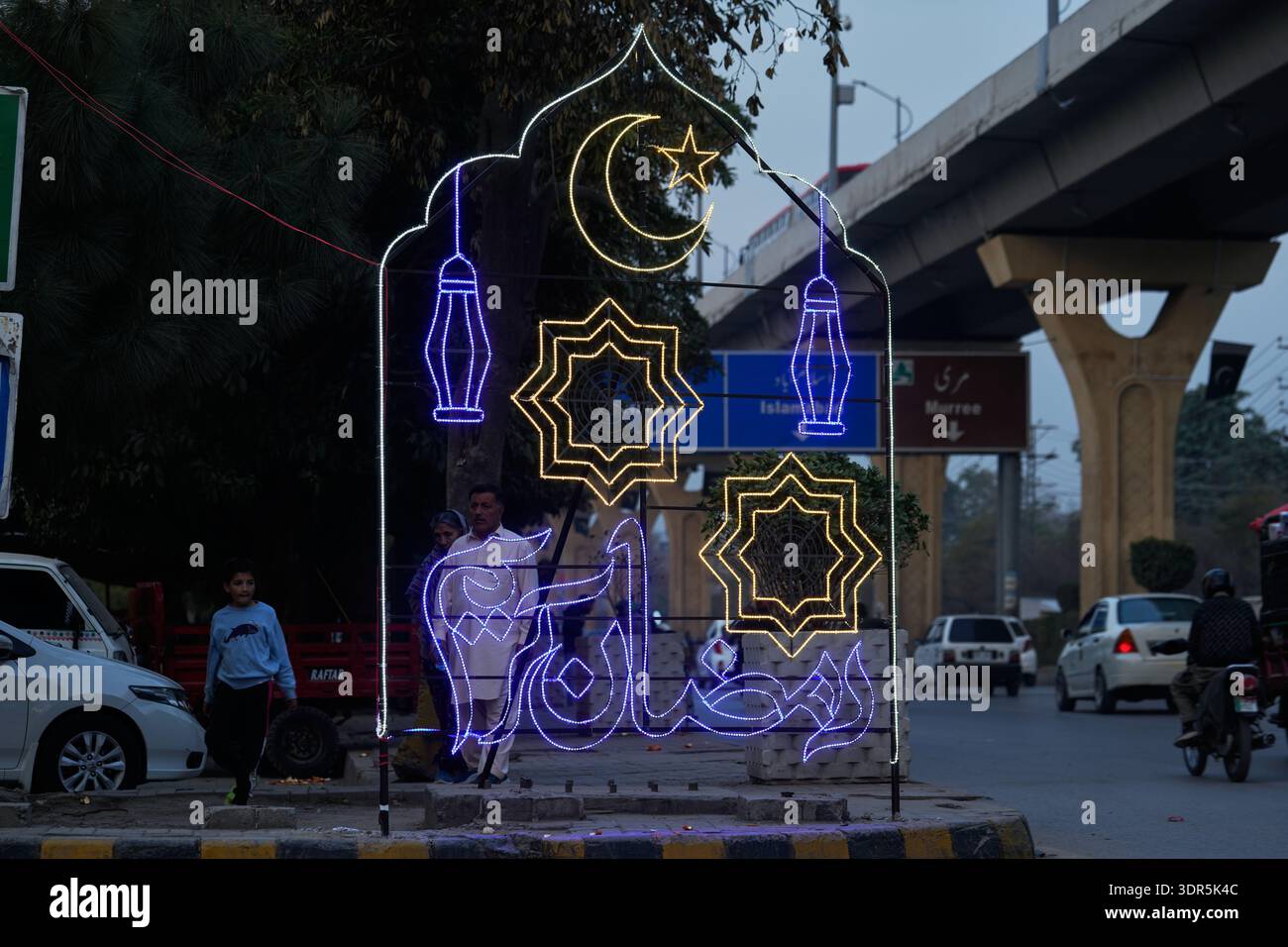 A family walk past a neon light decoration with wording 'Ramadan Kareem ...