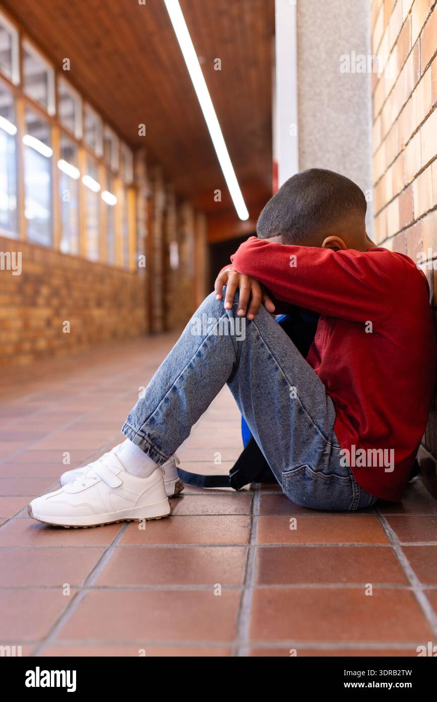 Sitting in school hallway, boy leaning against wall, feeling sad ...
