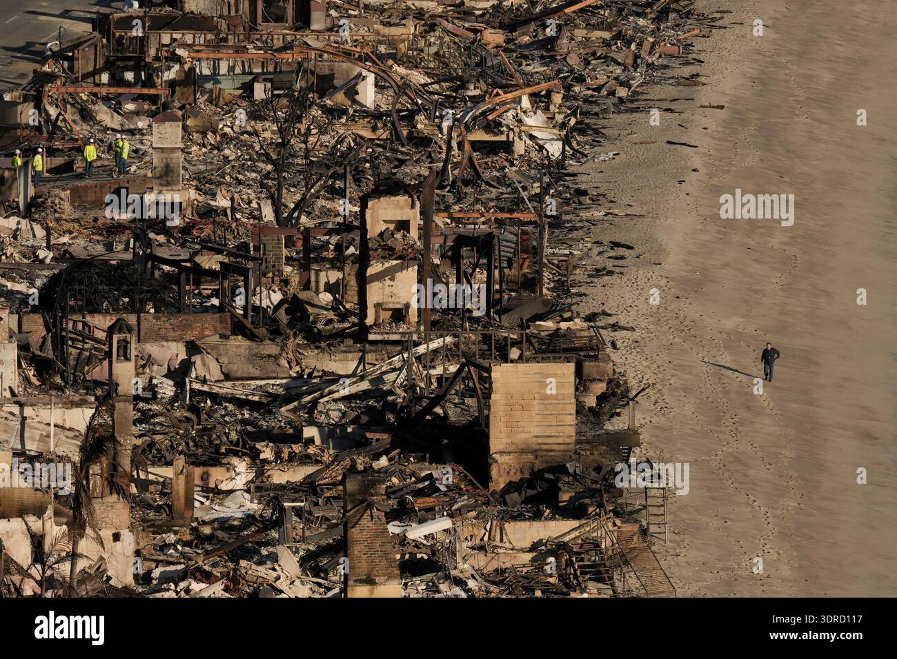 FILE - A person walks on the beach next to homes damaged by the ...