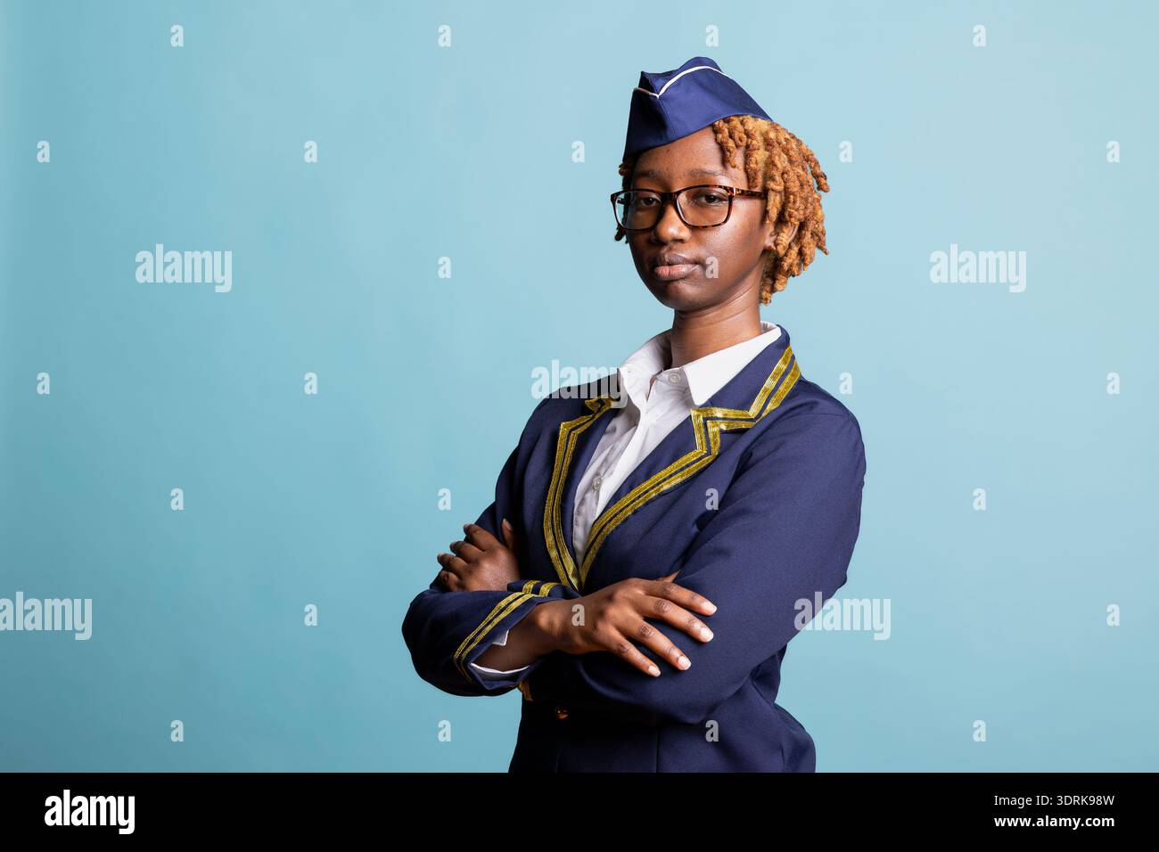 Portrait of black air hostess in blue and gold uniform crossing arms ...