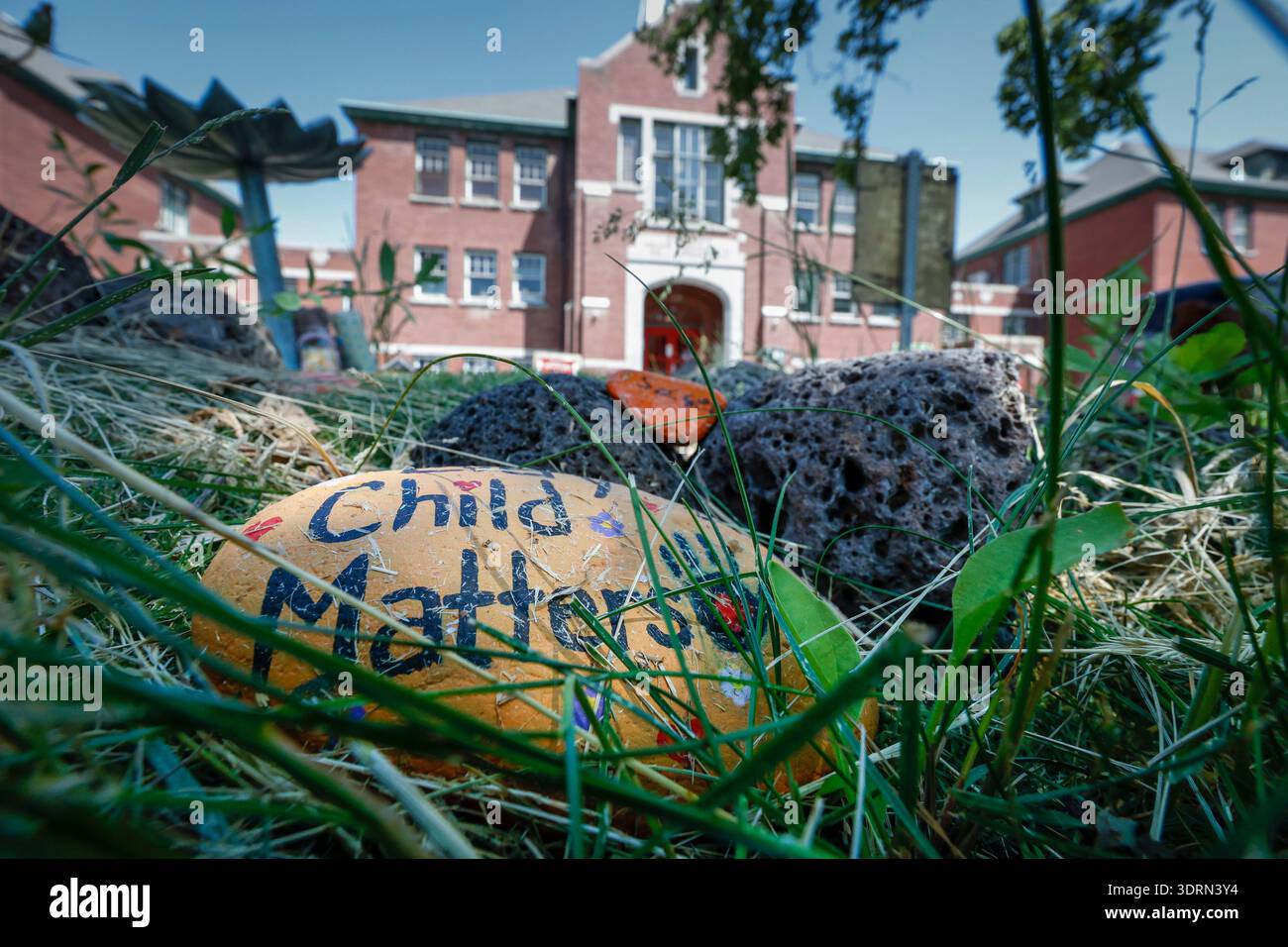 A hand-painted stone lies in the grass at a memorial outside the former ...