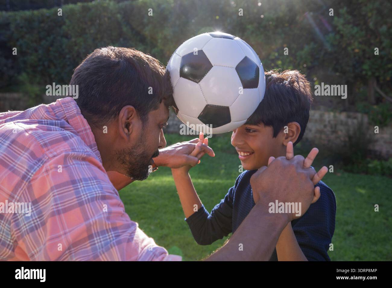 Indian father and son pressing soccer ball between foreheads while ...