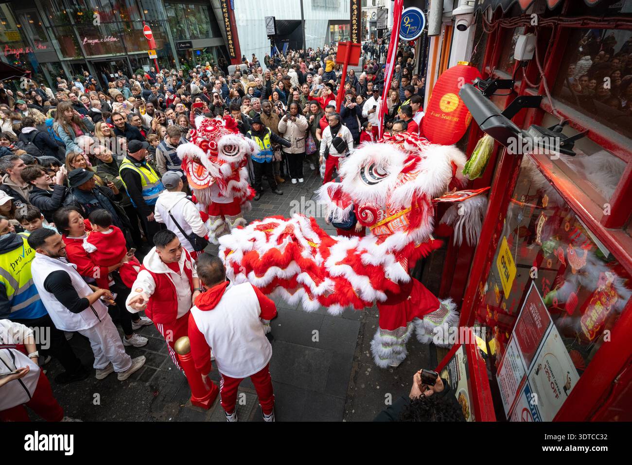 Performers in lion costume is grabbing a lettuce hanging on the shop ...