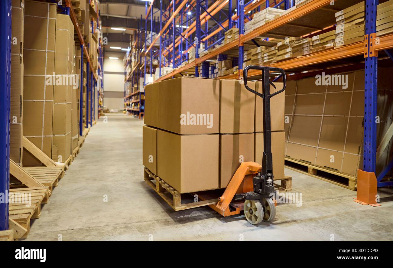 Warehouse aisle with pallet trolley moving boxes on racks for storage ...