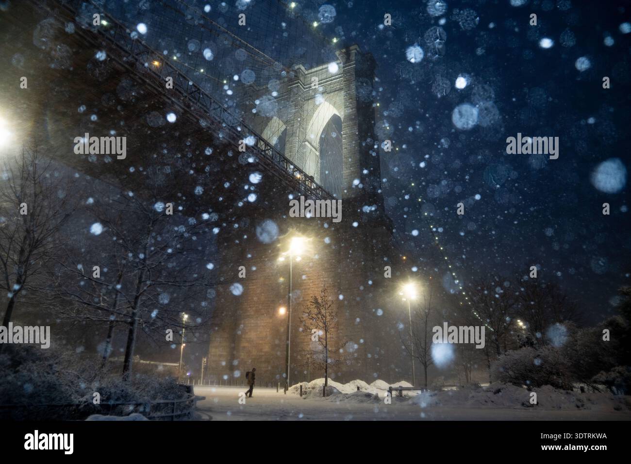 A pedestrian walks below the Brooklyn Bridge as snow falls during a ...