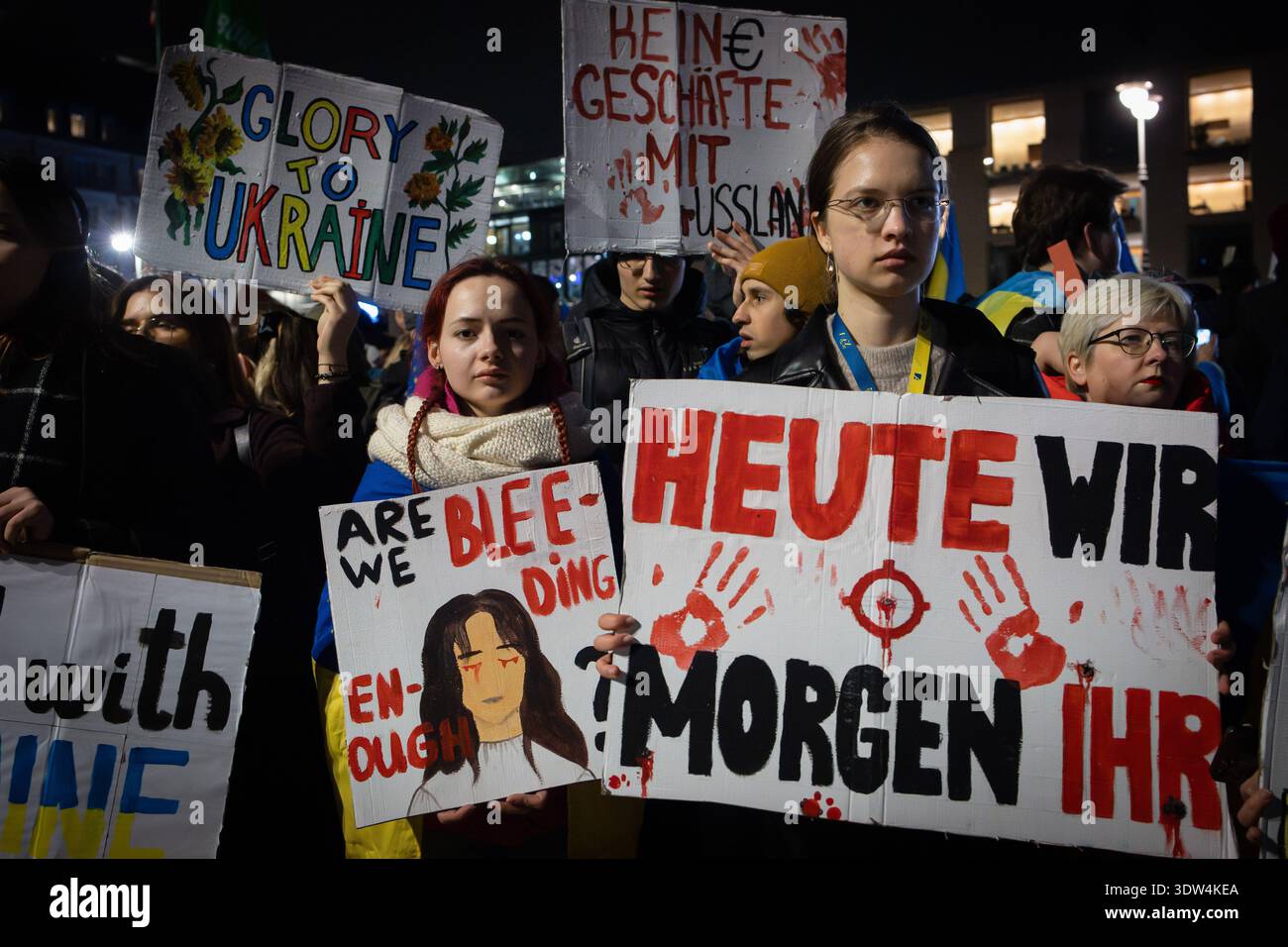 A group of young women hold anti-war placards and Ukrainian flags ...