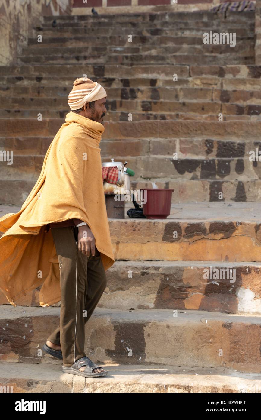 Chai vendor wrapped in warm clothing walking on stone steps in Varanasi ...