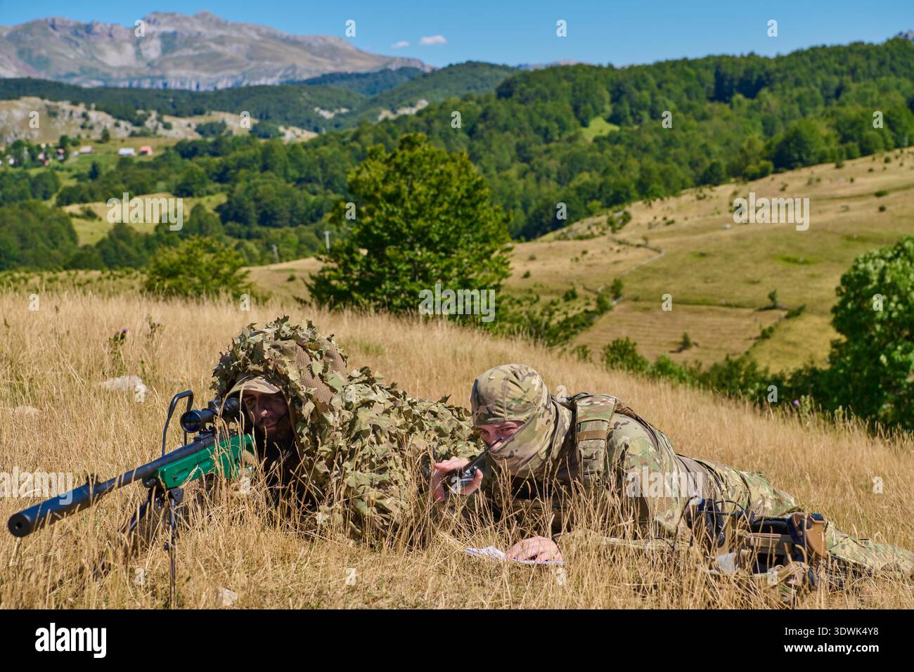 Two military snipers in full camouflage and tactical gear lie prone in ...