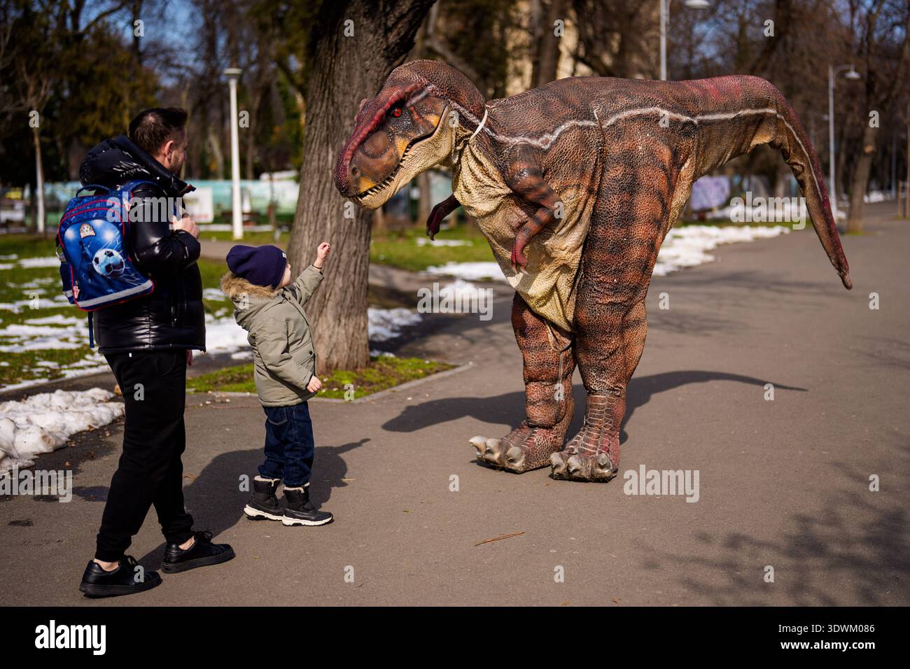 David, 6 years-old, reaches to a person in a dinosaur costume outside a ...