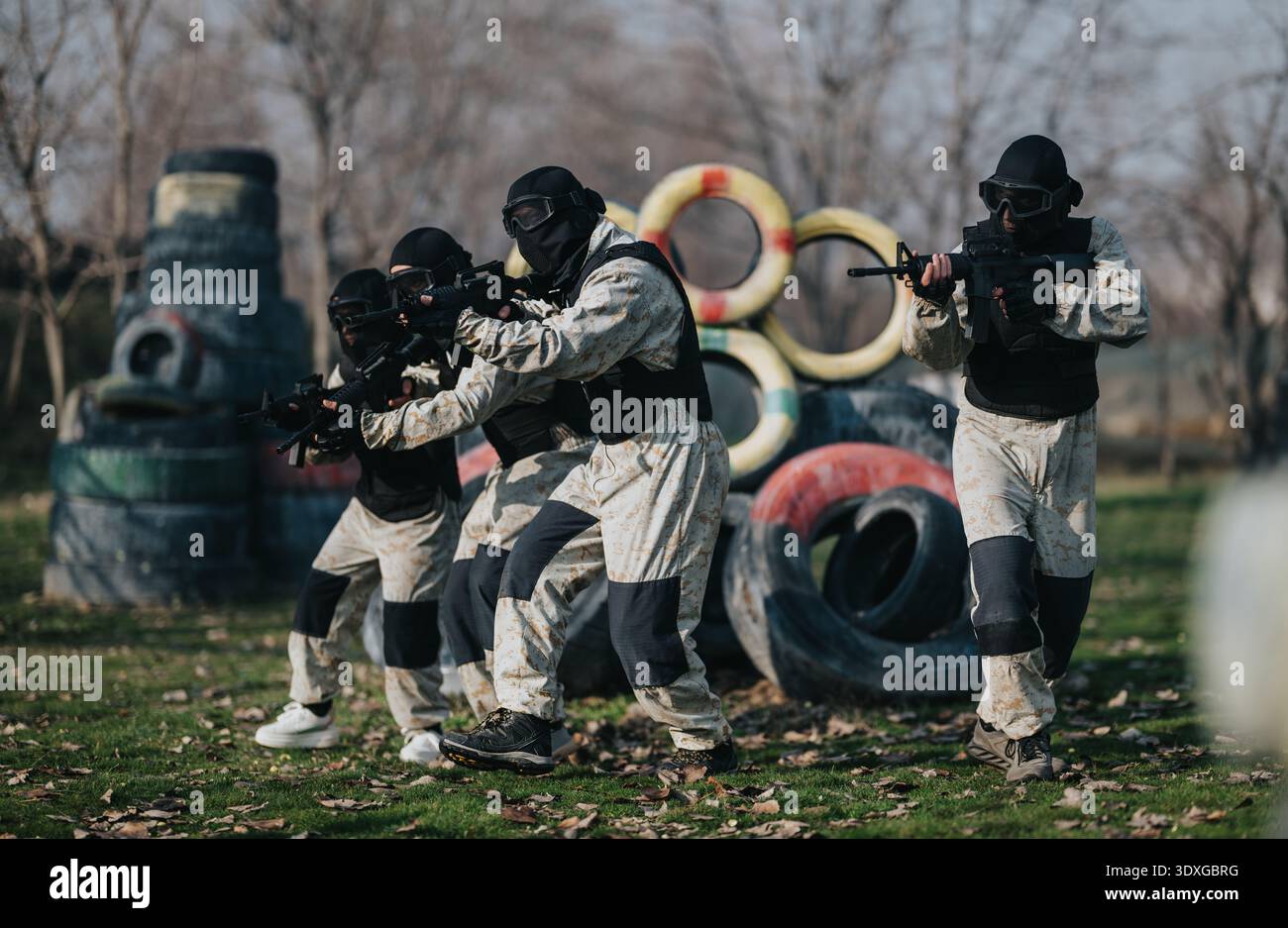 Paintball team crouching and aiming rifles in outdoor arena with tires ...