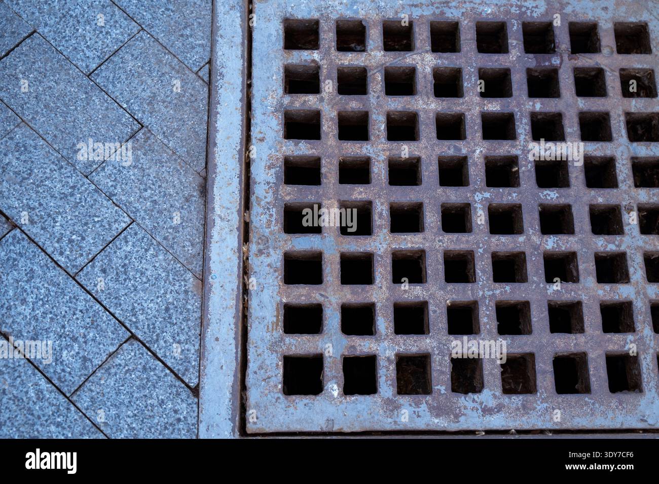Iron storm drain grate on a granite tiled sidewalk for rain water ...