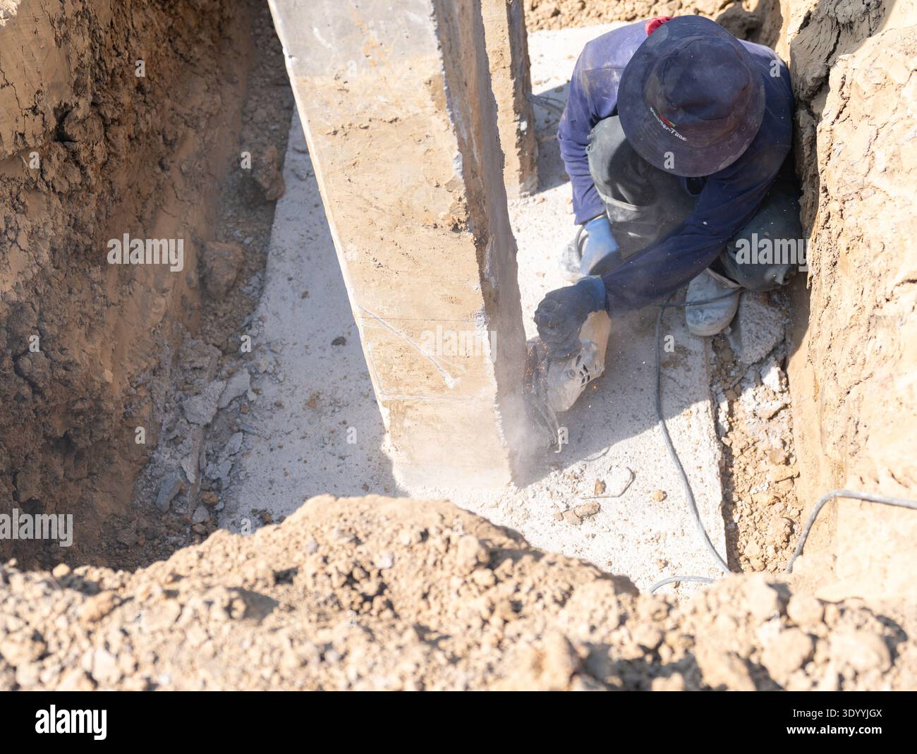 A laborer in a work hat uses an angle grinder to cut through a concrete ...