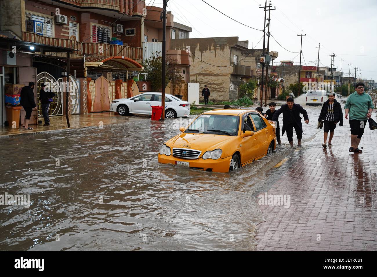 People push a car through a flooded street in Mosul after heavy rains ...