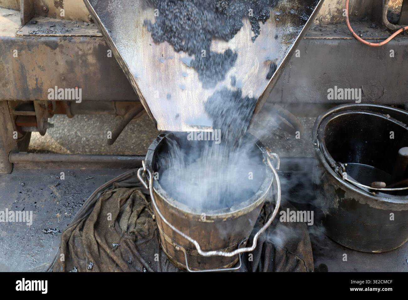 Asphaltkocher im Arbeitseinsatz Heißer Gussasphalt wird in einem Eimer ...