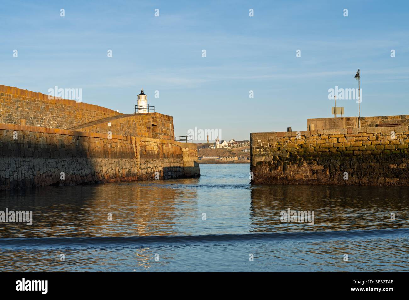 Golden light bathes the sturdy stone harbor entrance walls and the ...