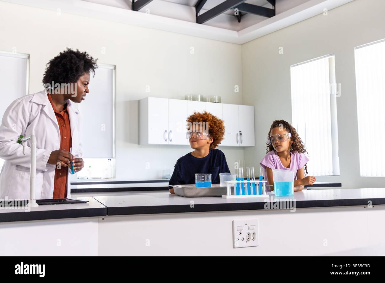 African American teacher in lab coat instructing two children in lab ...