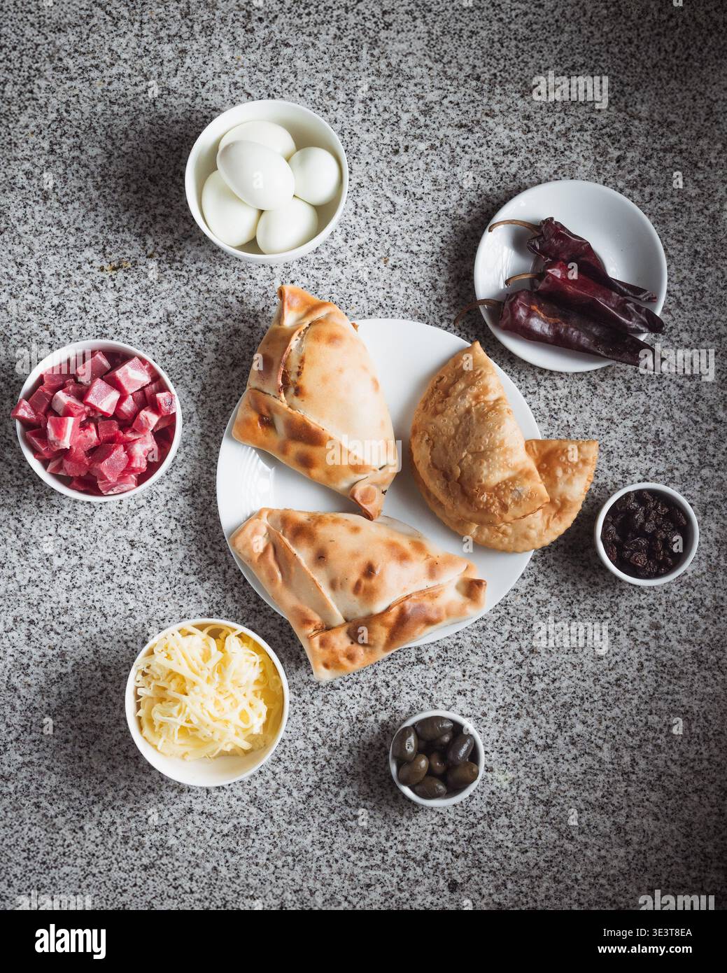 Flaky pastries rest on a white plate. Small bowls hold eggs, cheese ...