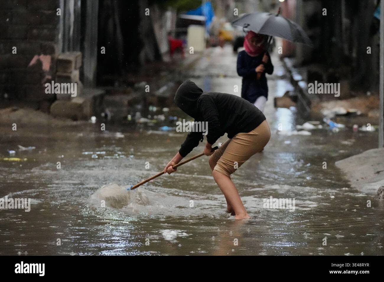 A Iraqi cleans rain water from a flooded street after heavy rain fell ...