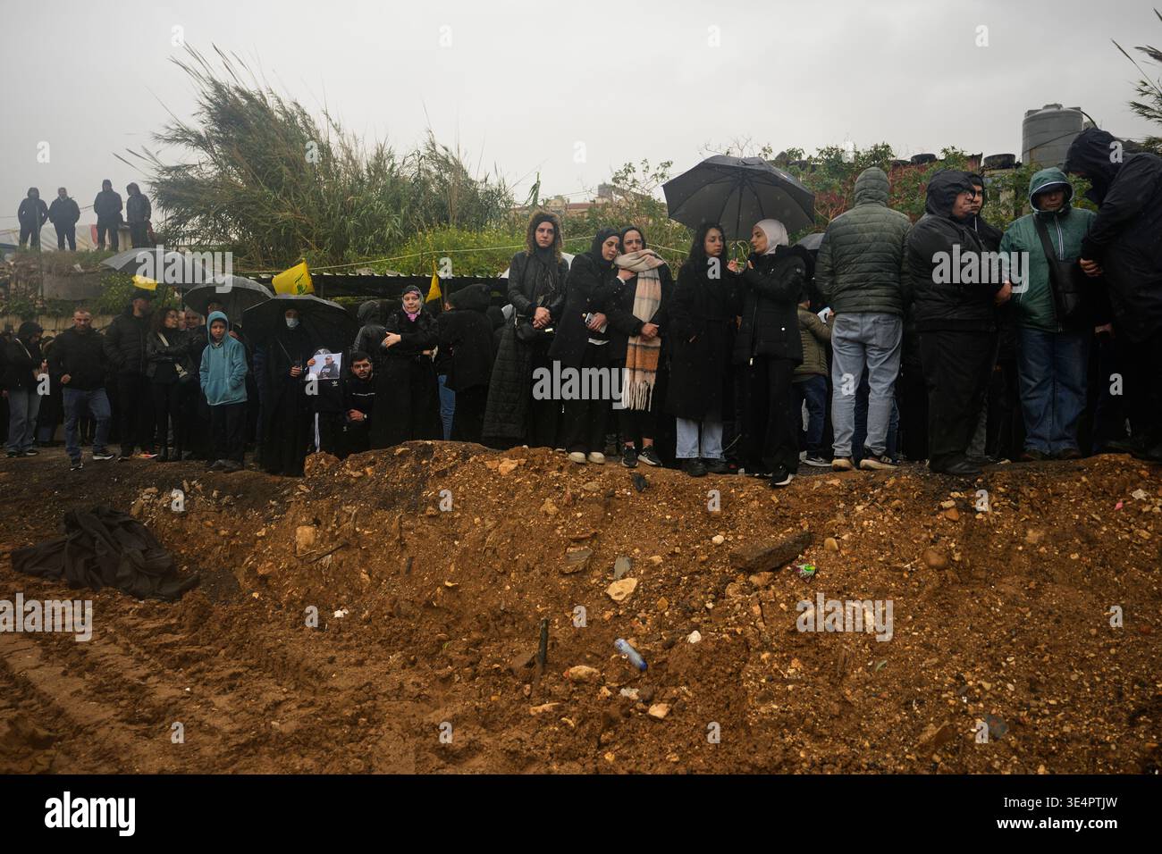 Mourners gather near a freshly dug grave during the funeral of ...