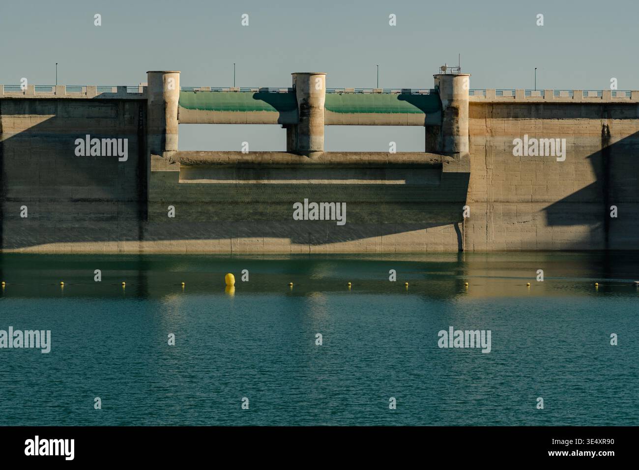 Wide view of a massive concrete dam wall featuring green spillway gates ...