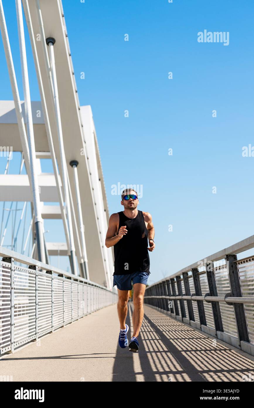 Urban male athlete jogging on a modern city bridge: a front view of a ...