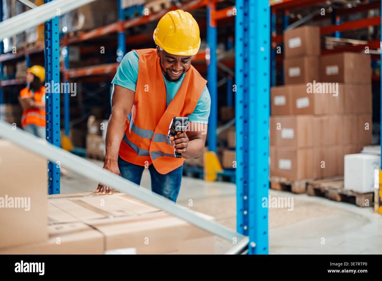 Black male worker wearing hard hat and safety vest scanning boxes using ...