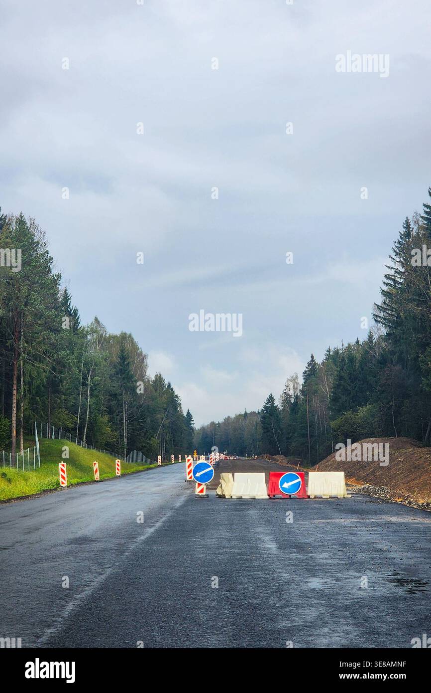 Asphalt road under construction with barriers and traffic signs ...