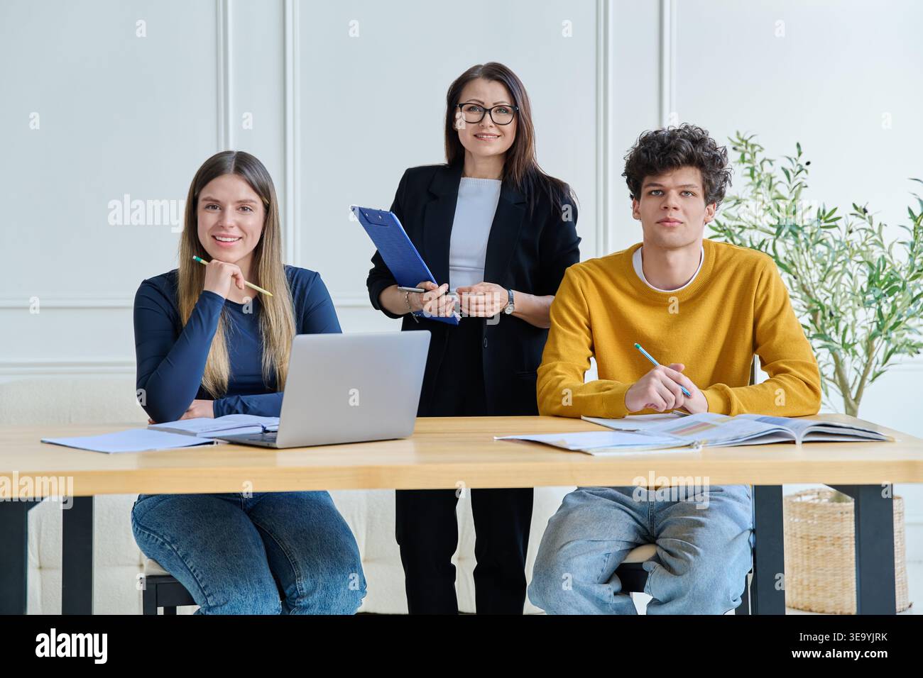 Two university students with female teacher mentor study while sitting ...