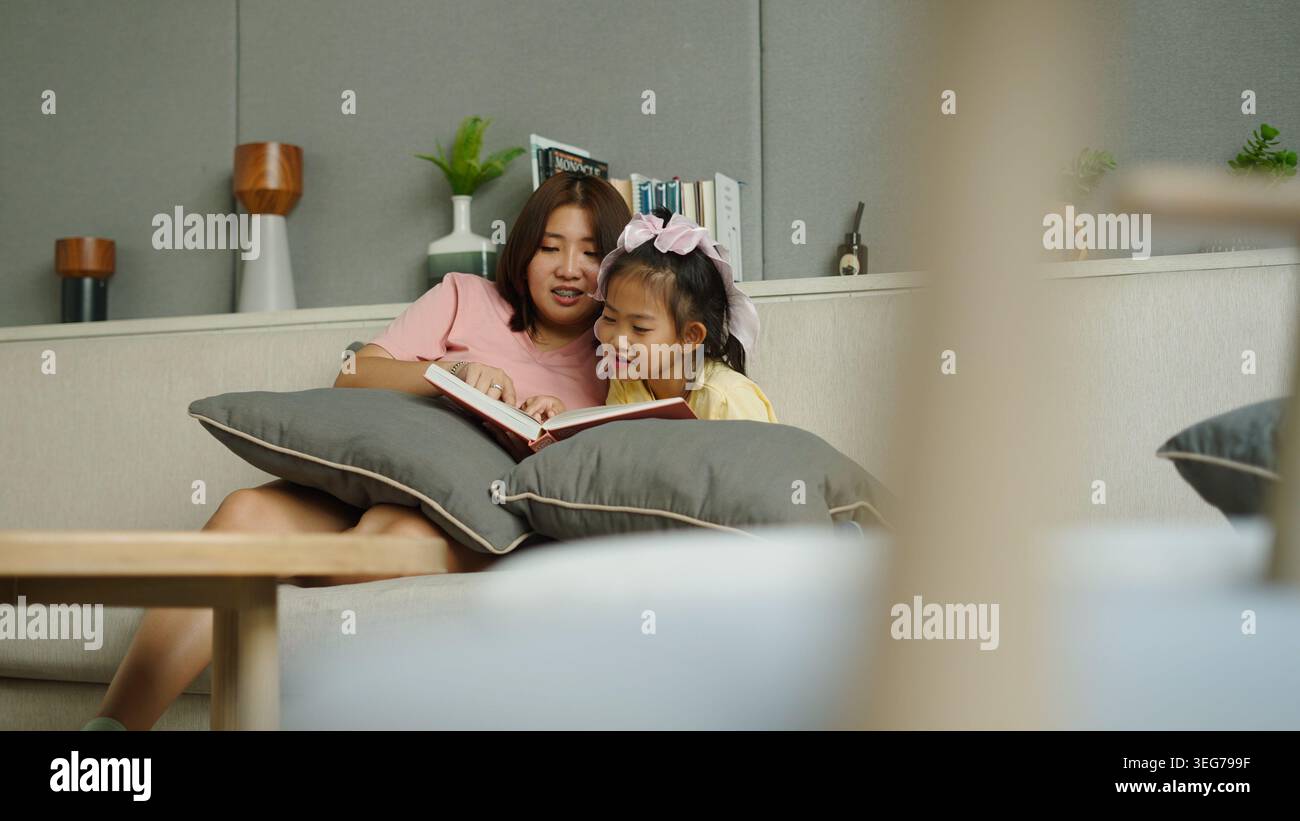 Mother and daughter reading book on sofa, enjoying quality family ...