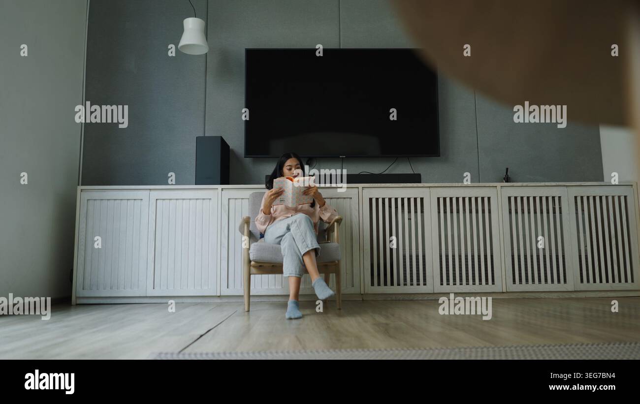 Young woman reading book in living room, enjoying quiet home moment ...