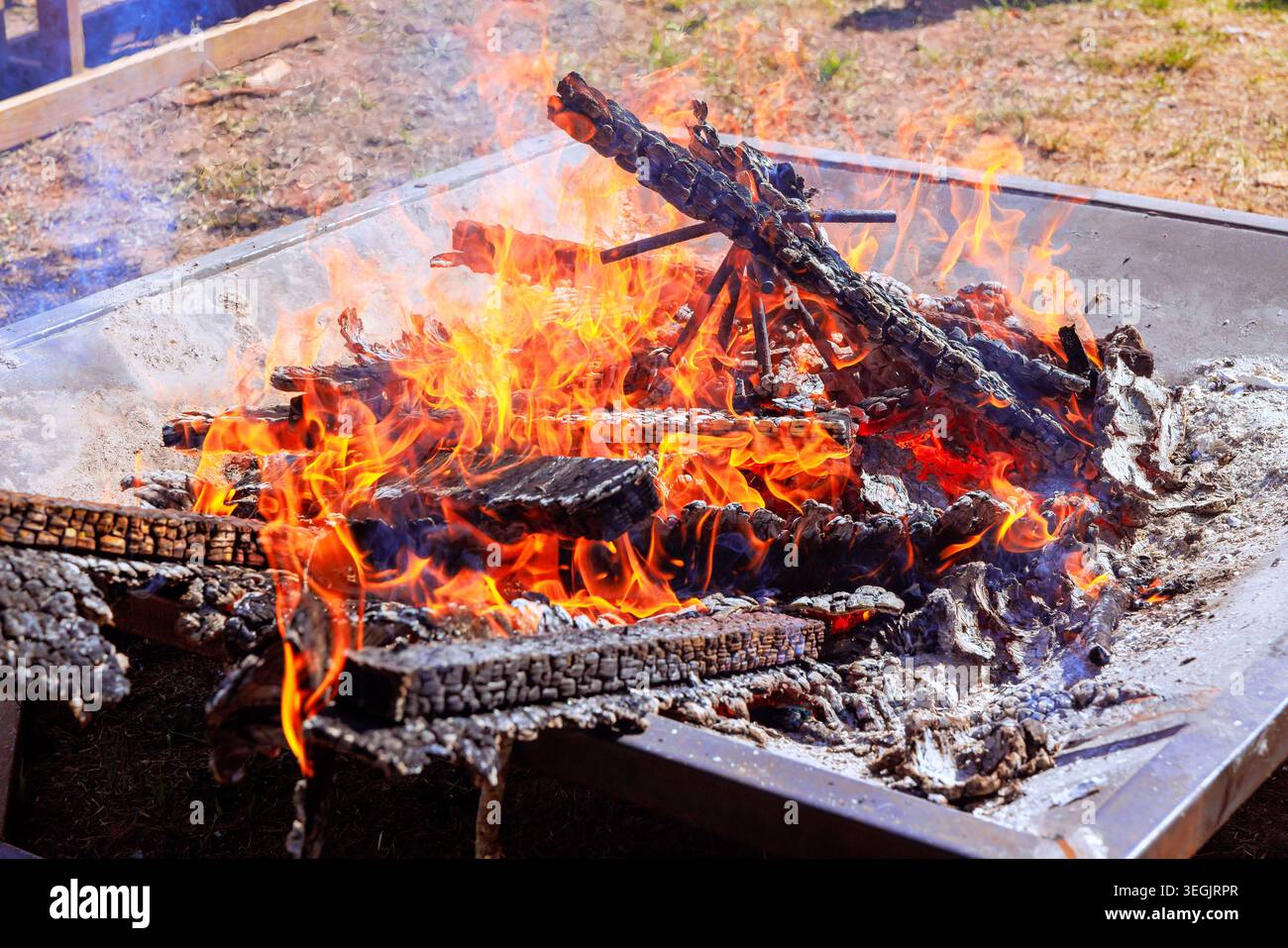 Bright flames rise from burning wood in metal fire pit under sun at ...