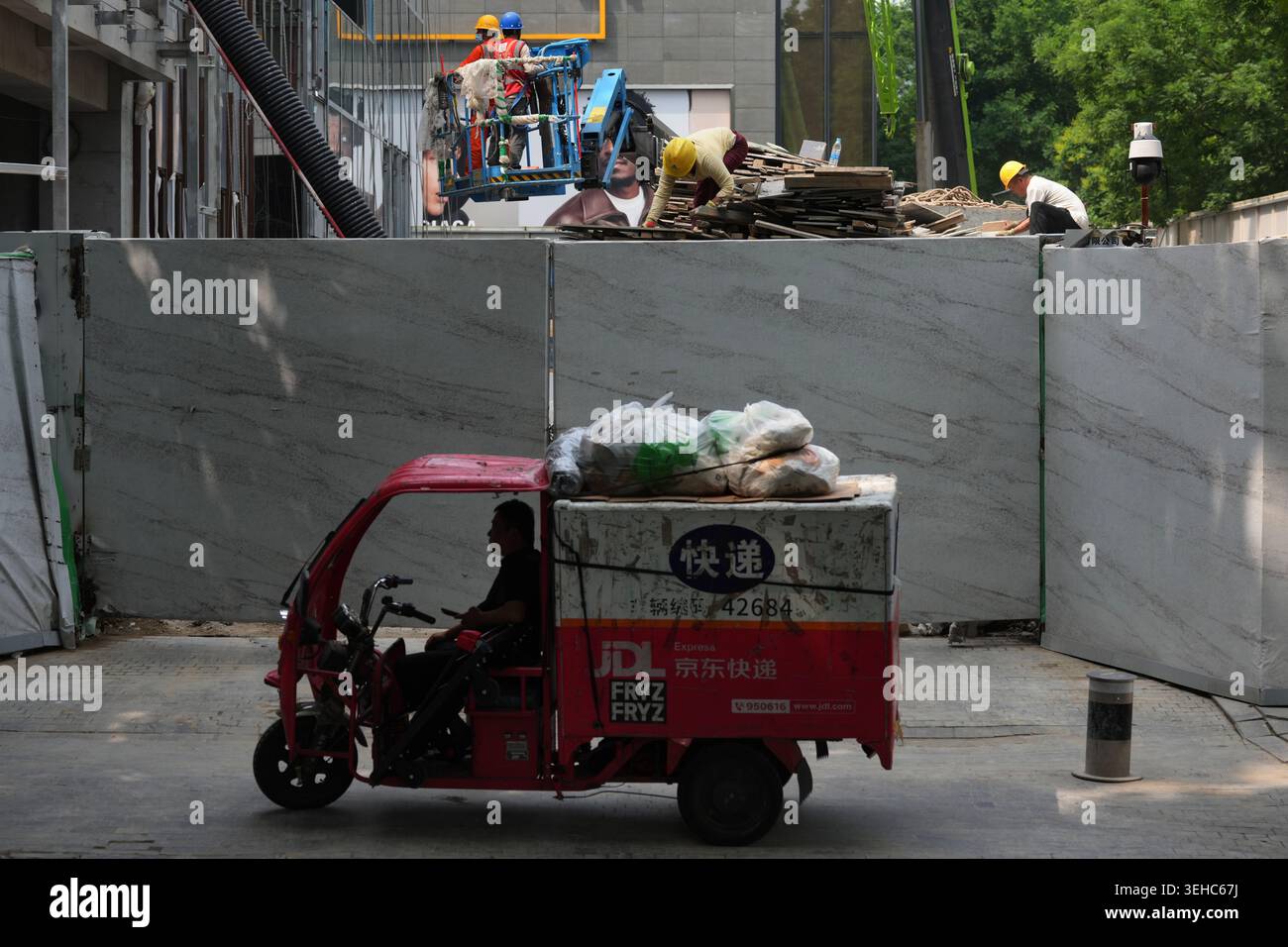A delivery courier rests on his cart as workers labor at a construction ...
