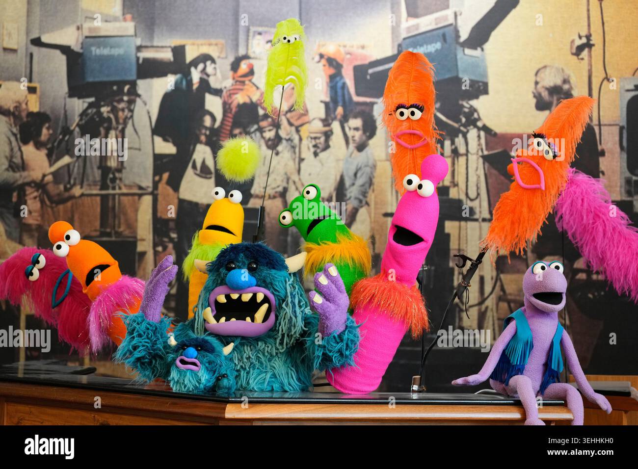 Puppets are displayed in front of a photo of puppeteers working on ...