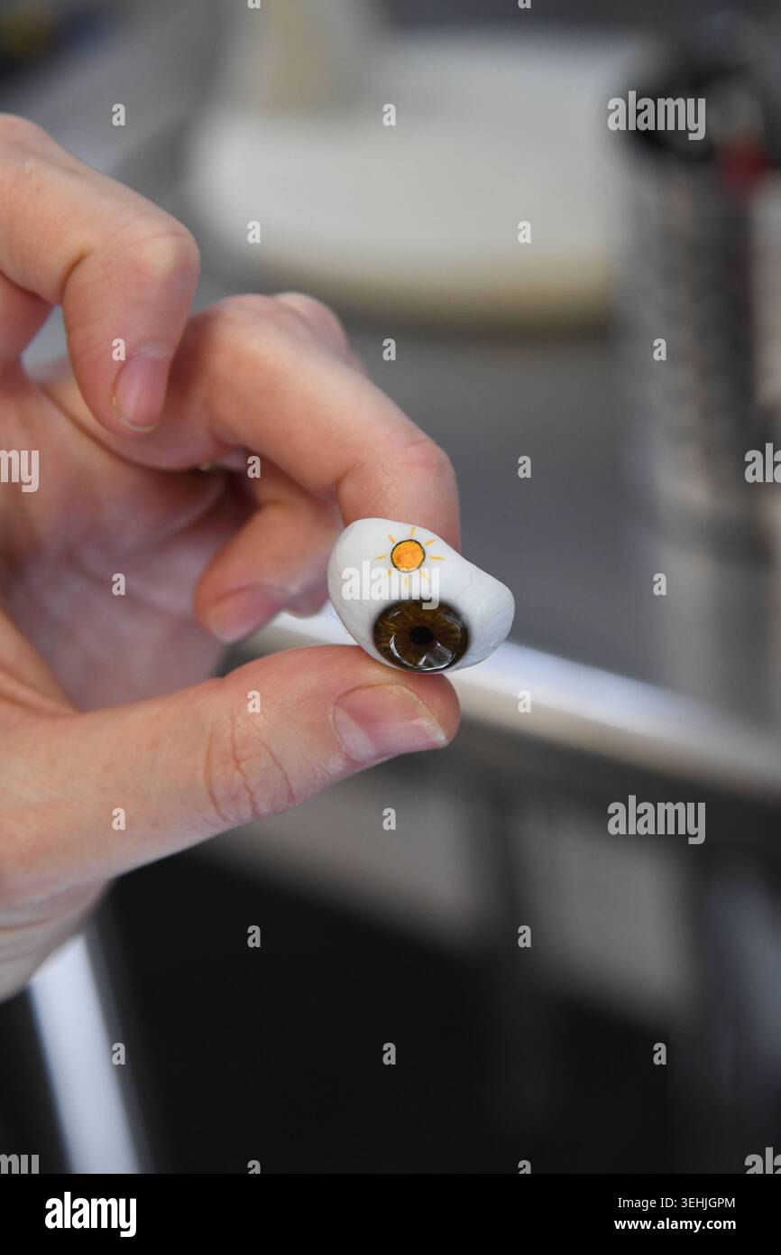 One hand holds a custom-made prosthetic eye featuring a brown iris and ...