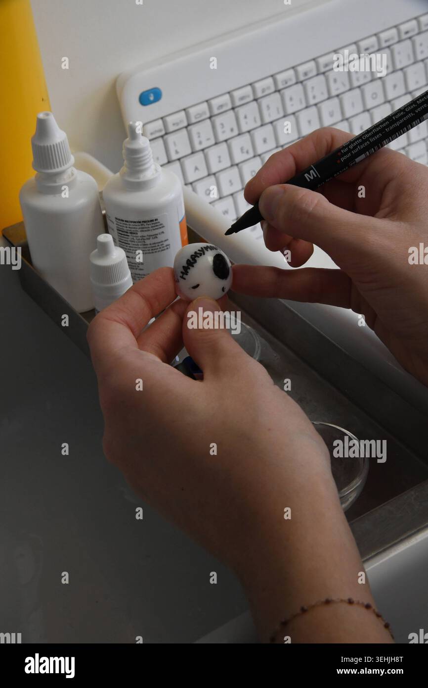 Ocularist using a black marker to write on a small white spherical ...