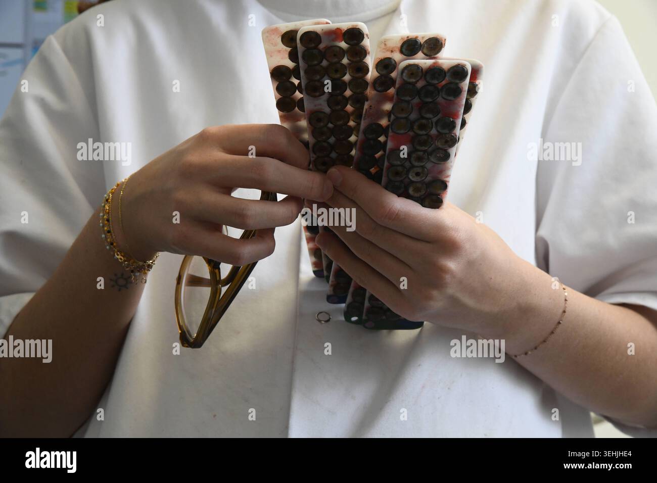 A person in a white coat holds several white plates containing multiple ...