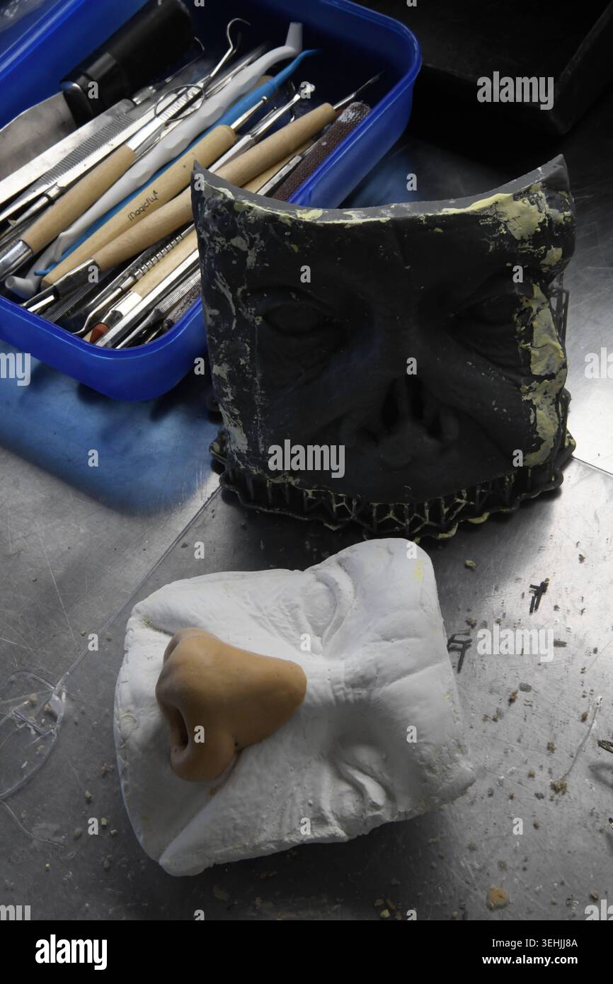 A blue tool tray is placed next to a dark face mold and a white plaster ...