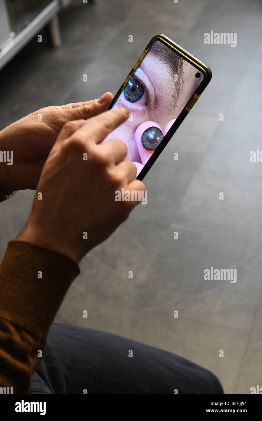Ocularist holding a smartphone displaying a close-up photo of a human ...
