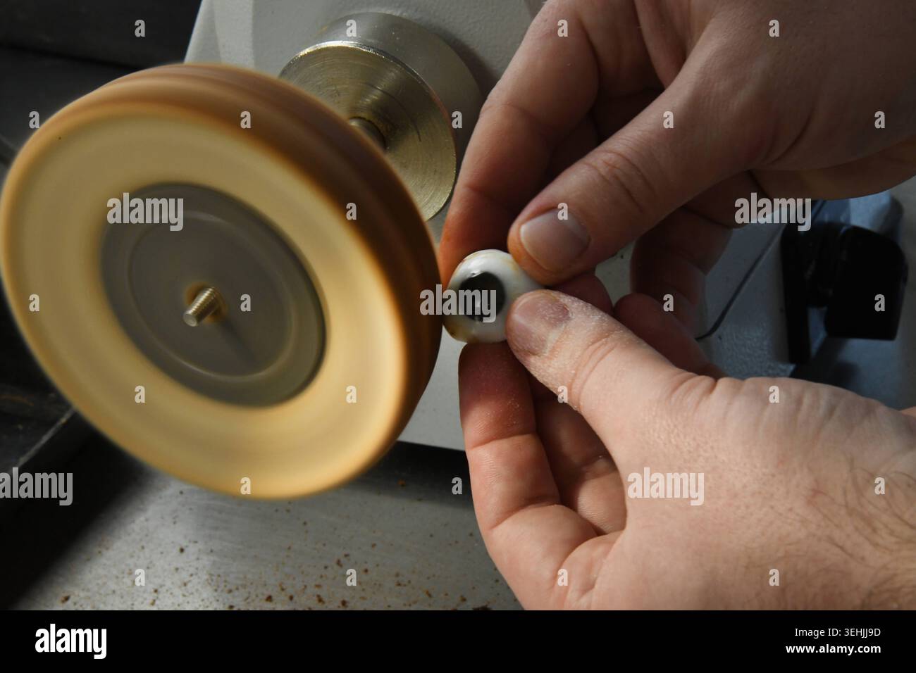 Ocularist holding a prosthetic eye against a polishing wheel ...