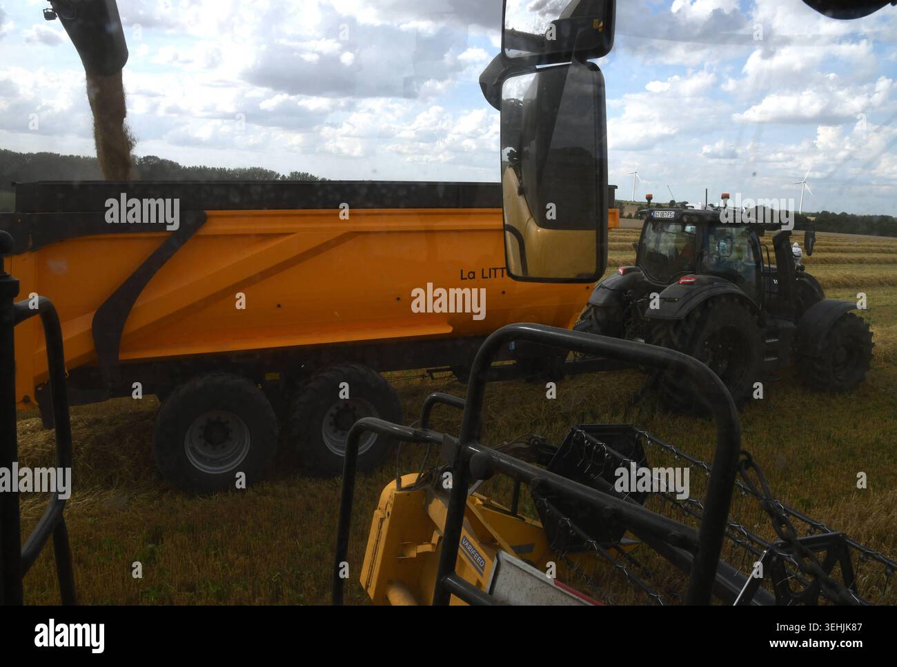 A black tractor pulls a yellow trailer being filled with grain from an ...