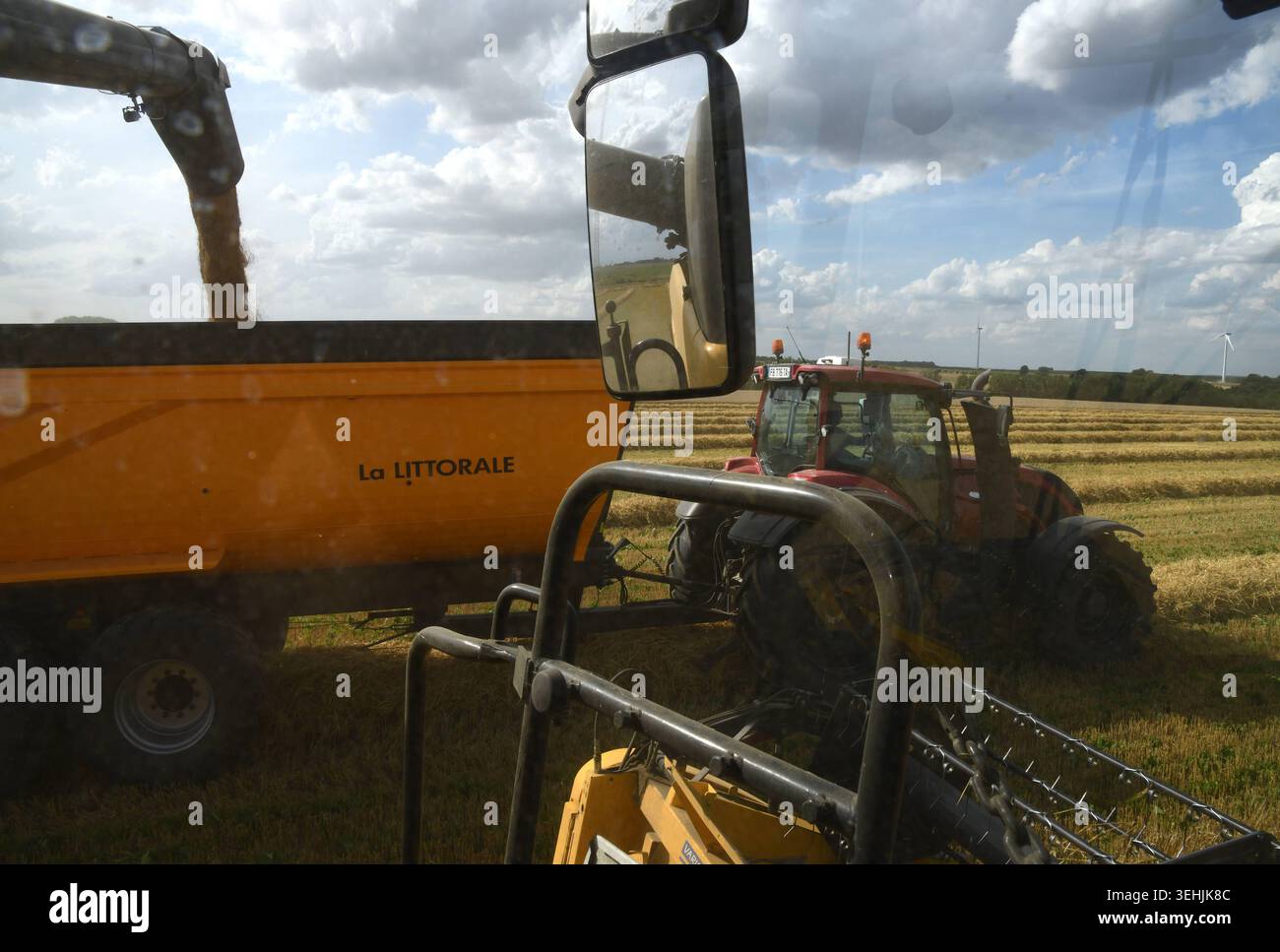 A combine harvester pours grain into a yellow trailer pulled by a red ...