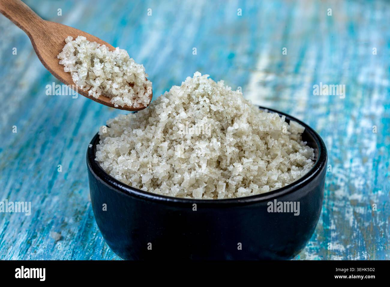 A black bowl filled with coarse white crystals sits on a blue wooden ...