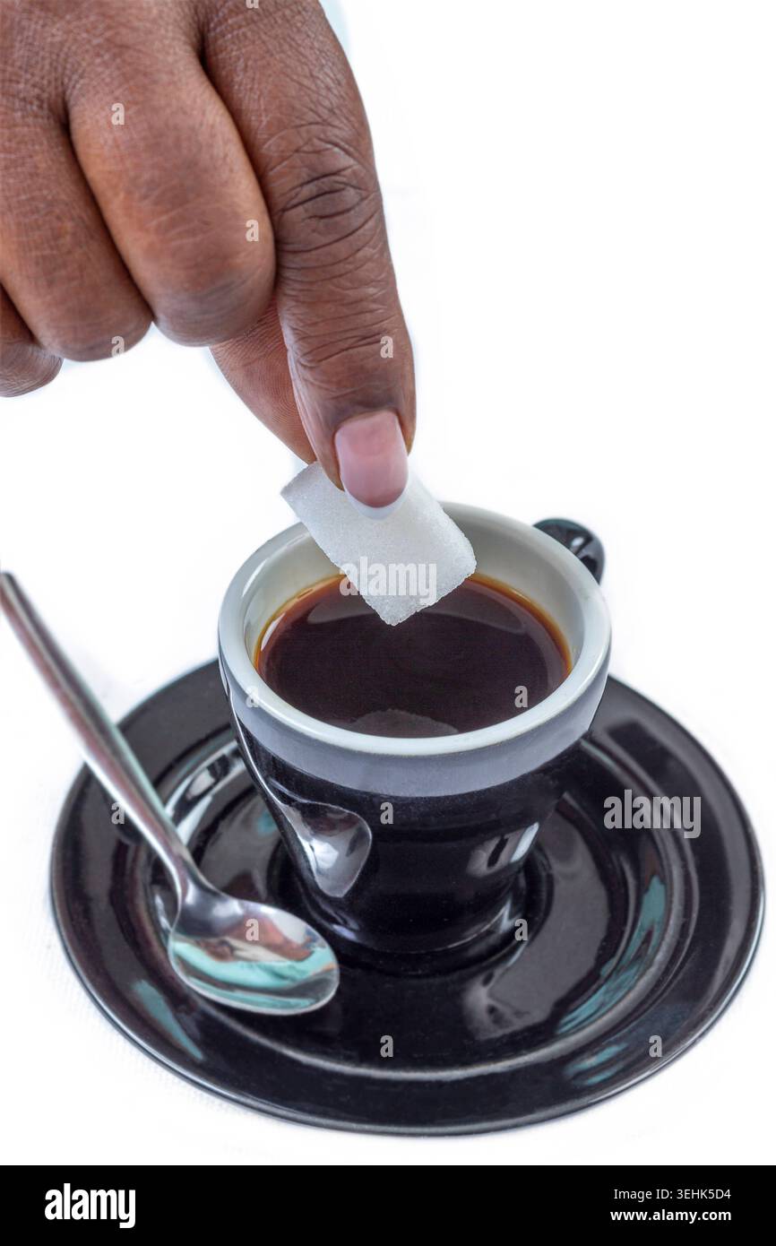 A hand holds a white sugar cube over a small cup of black coffee. The ...
