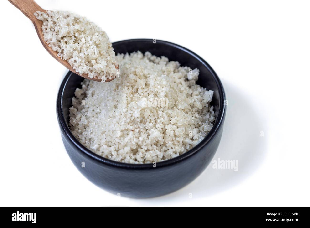 A black bowl is filled with white crystals. A wooden spoon holds a ...